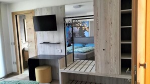 Quarto moderno com televisão na parede, cama com cabeceira azul e guarda-roupa de madeira com espelho.