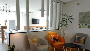 Uma sala de estar moderna com um sofá, poltronas e uma mesa de centro. Há uma planta, uma pequena mesa com um vaso e um mural na parede.