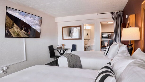 Quarto de hotel com duas camas, uma escrivaninha, uma cadeira, um abajur e um quadro na parede.