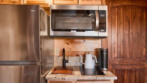 Uma cozinha compacta com geladeira de aço inoxidável, micro-ondas, cafeteira e armários de madeira.