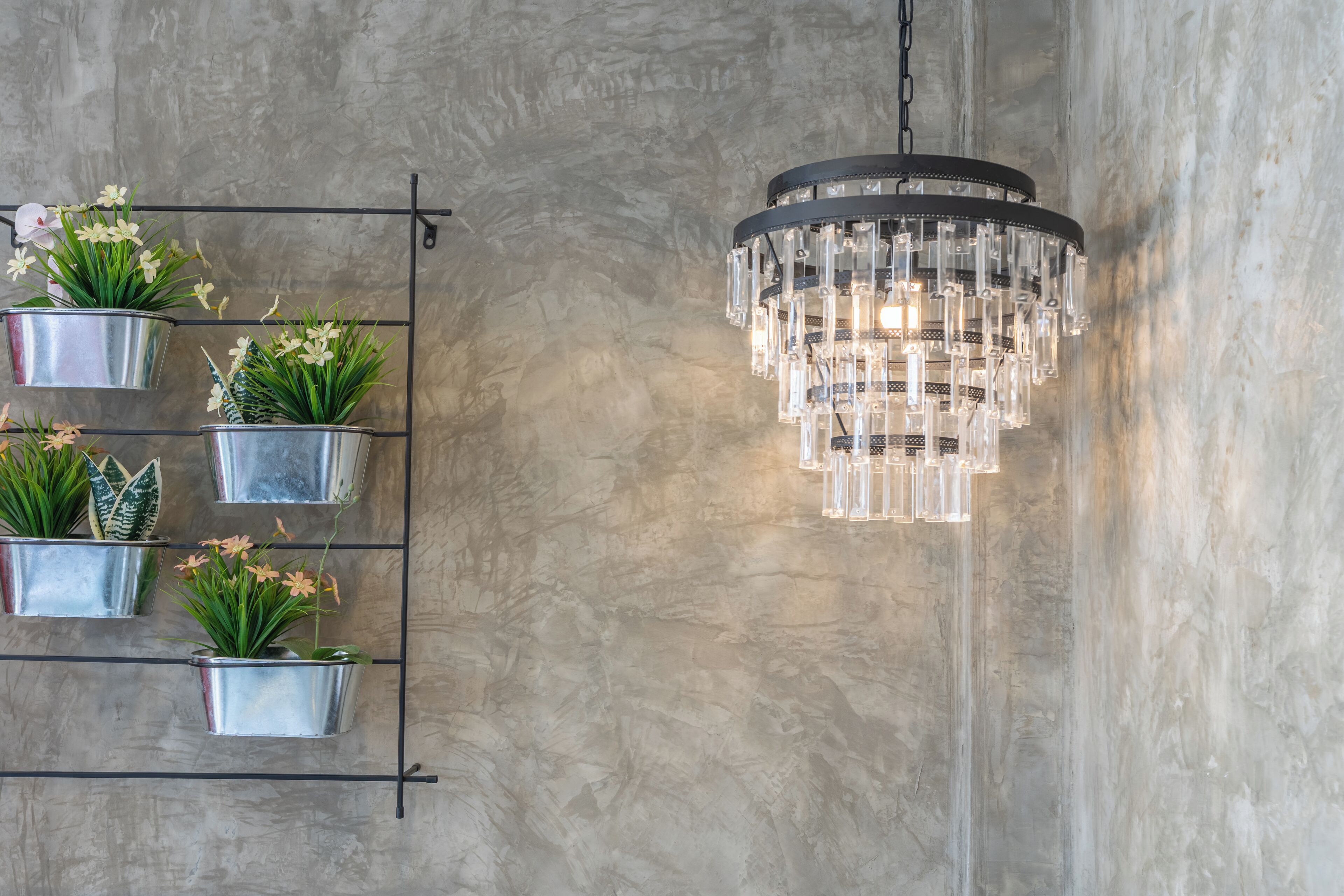Um candelabro pendurado no teto, uma estante com plantas fixada na parede e uma parede com textura.