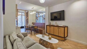 Uma sala de estar moderna com um sofá, uma área de jantar, uma TV fixada na parede e um armário de madeira.