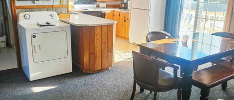 Uma cozinha compacta com armários de madeira, fogão embutido, geladeira e uma janela grande com cortinas.