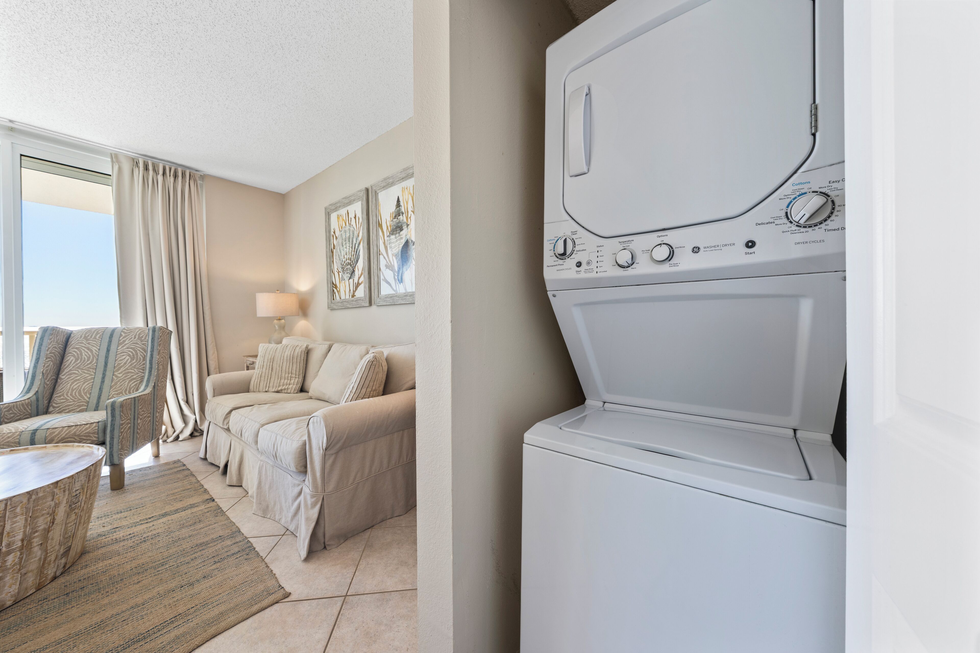 Quarto de hotel com sofá, mesa de centro, máquina de lavar e vista para o exterior.
