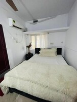 Quarto com cama, mesa de cabeceira, janela com cortinas e ar condicionado na parede.