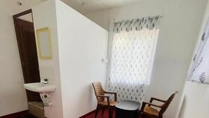 Quarto compacto com piso vermelho, pia branca, duas cadeiras de madeira e uma pequena mesa redonda.