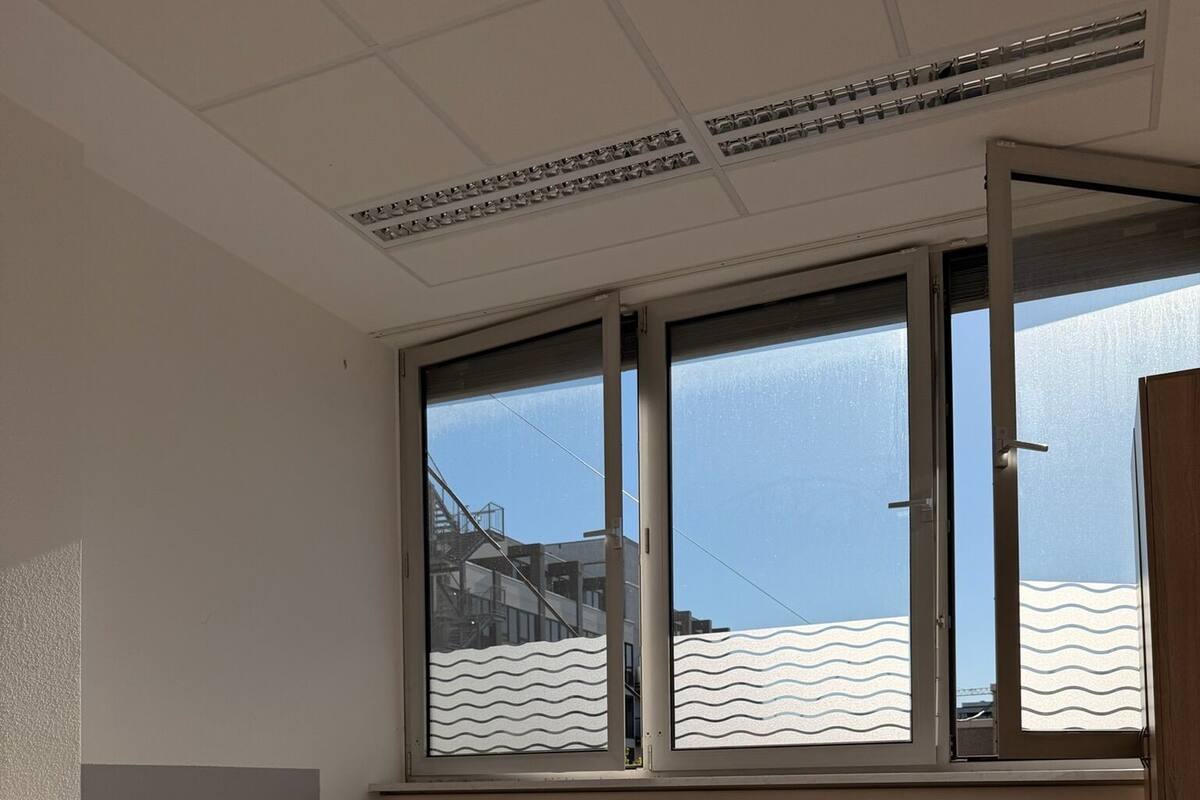 Quarto com duas camas, janela com vista para um edifício, radiador e uma pequena mesa de cabeceira.