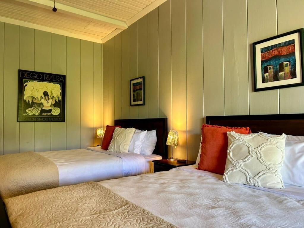 Quarto de hotel com duas camas, um quadro na parede e um cartaz de Diego Rivera.