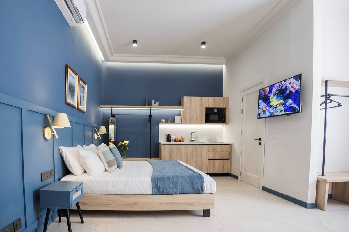 Quarto moderno com cama, mesa de cabeceira e televisão na parede.