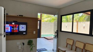 Um interior moderno com uma TV na parede, uma pequena planta e um espaço de estar com três cadeiras.