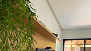 Uma sala de estar moderna com televisão na parede, estante de madeira e um vaso de planta.
