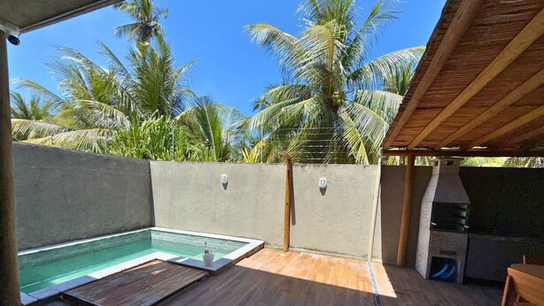 Piscina com deck de madeira, área de churrasco e vista para palmeiras.
