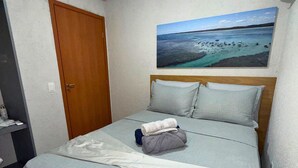 Um quarto com uma cama, uma porta, um quadro e uma mesa pequena com uma luminária.