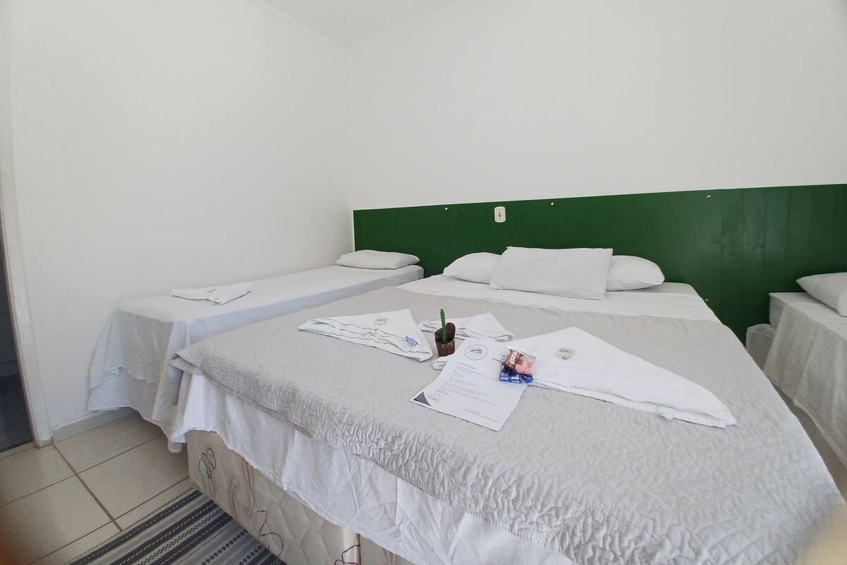 Quarto de hotel com duas camas de solteiro, cabeceira verde e chão ladrilhado.