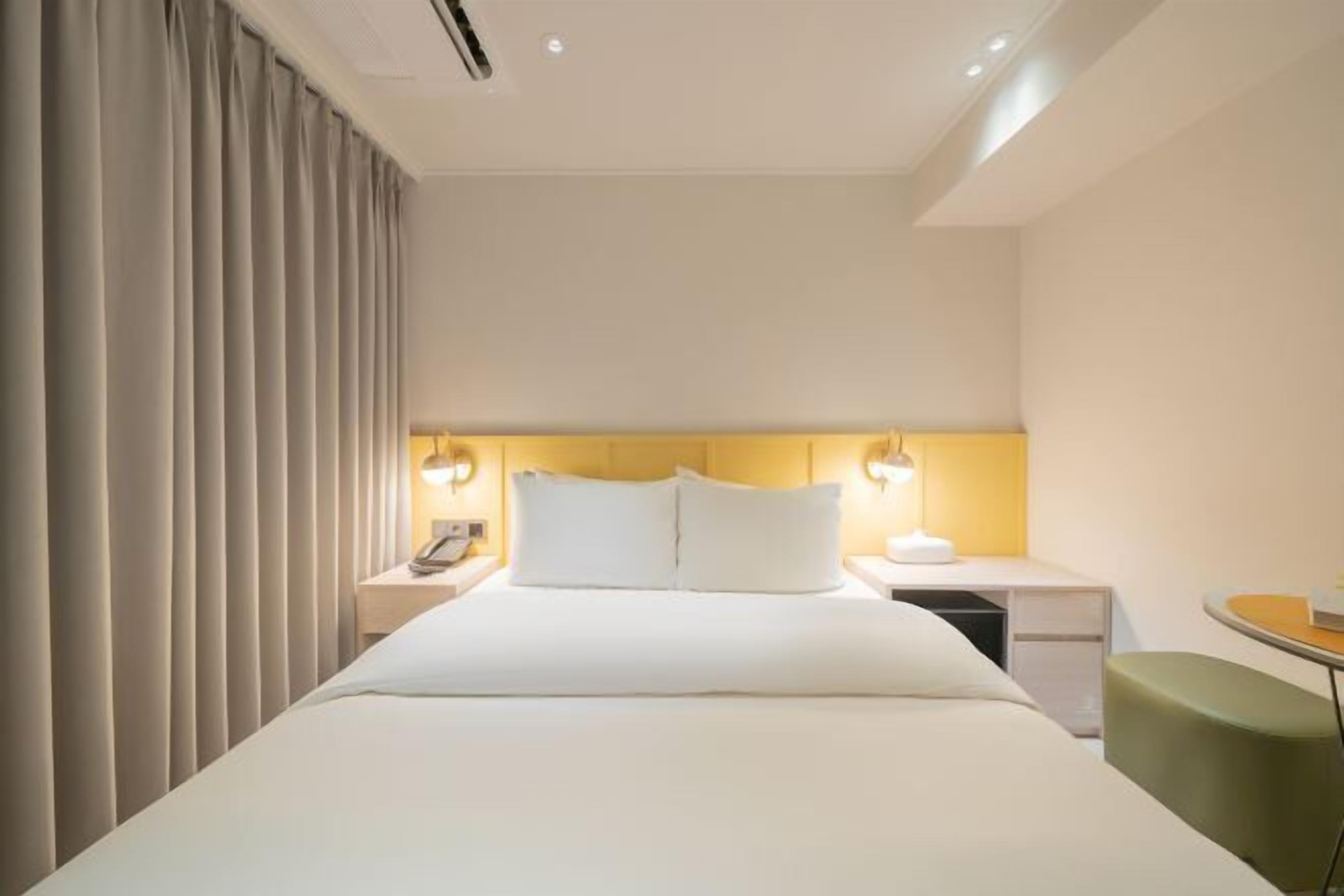 Quarto de hotel com uma cama grande, luminárias de cabeceira, uma escrivaninha e uma cadeira.