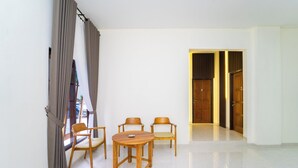 Quarto com uma mesa de jantar de madeira e cadeiras, uma janela com cortinas e uma porta que dá para outro cômodo.