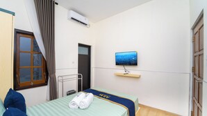 Quarto de hotel com cama, televisão fixada na parede, janela com cortinas e aparelho de ar condicionado.