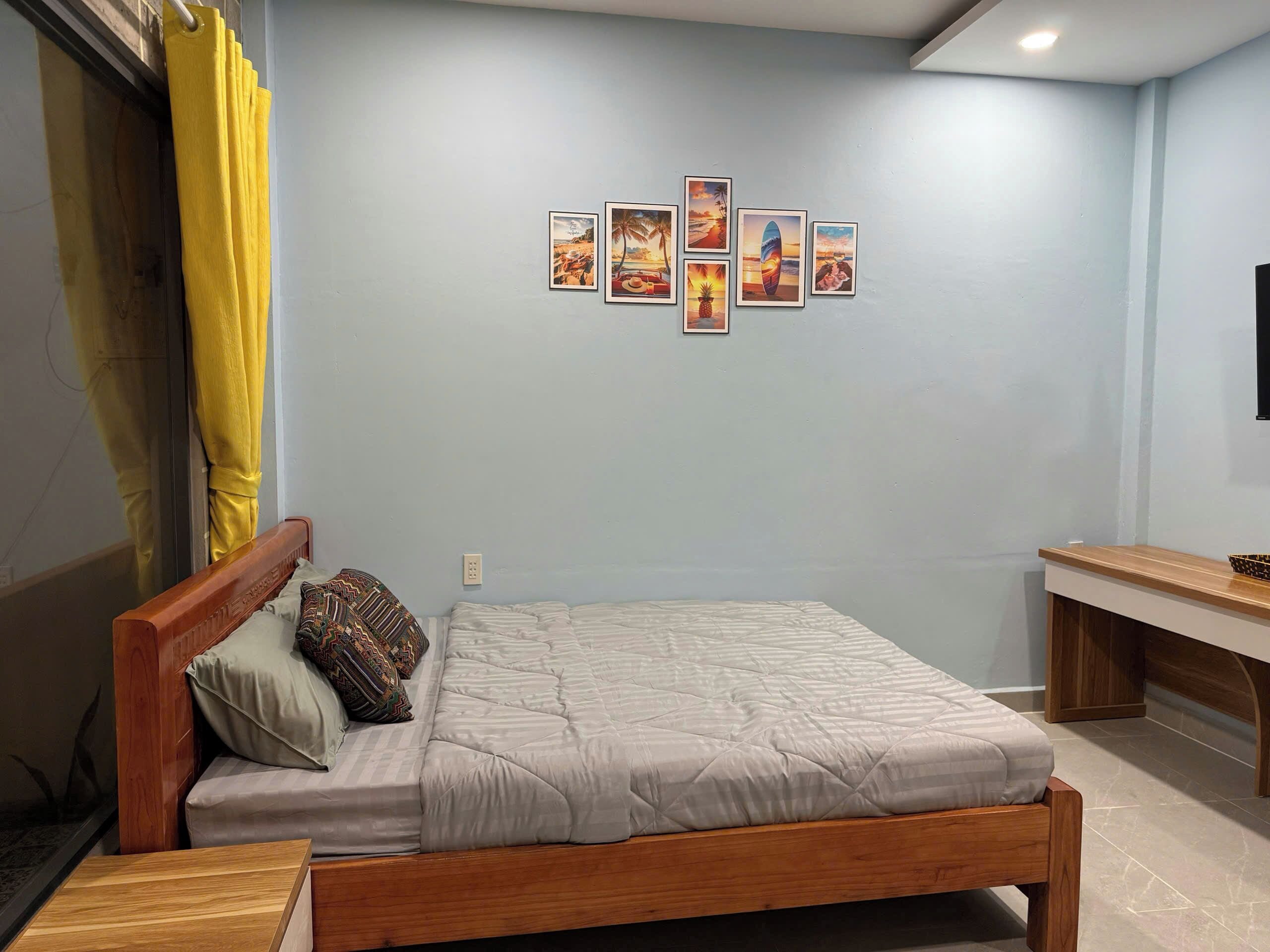 Quarto com uma cama, mesa de cabeceira, escrivaninha e parede com cinco quadros.