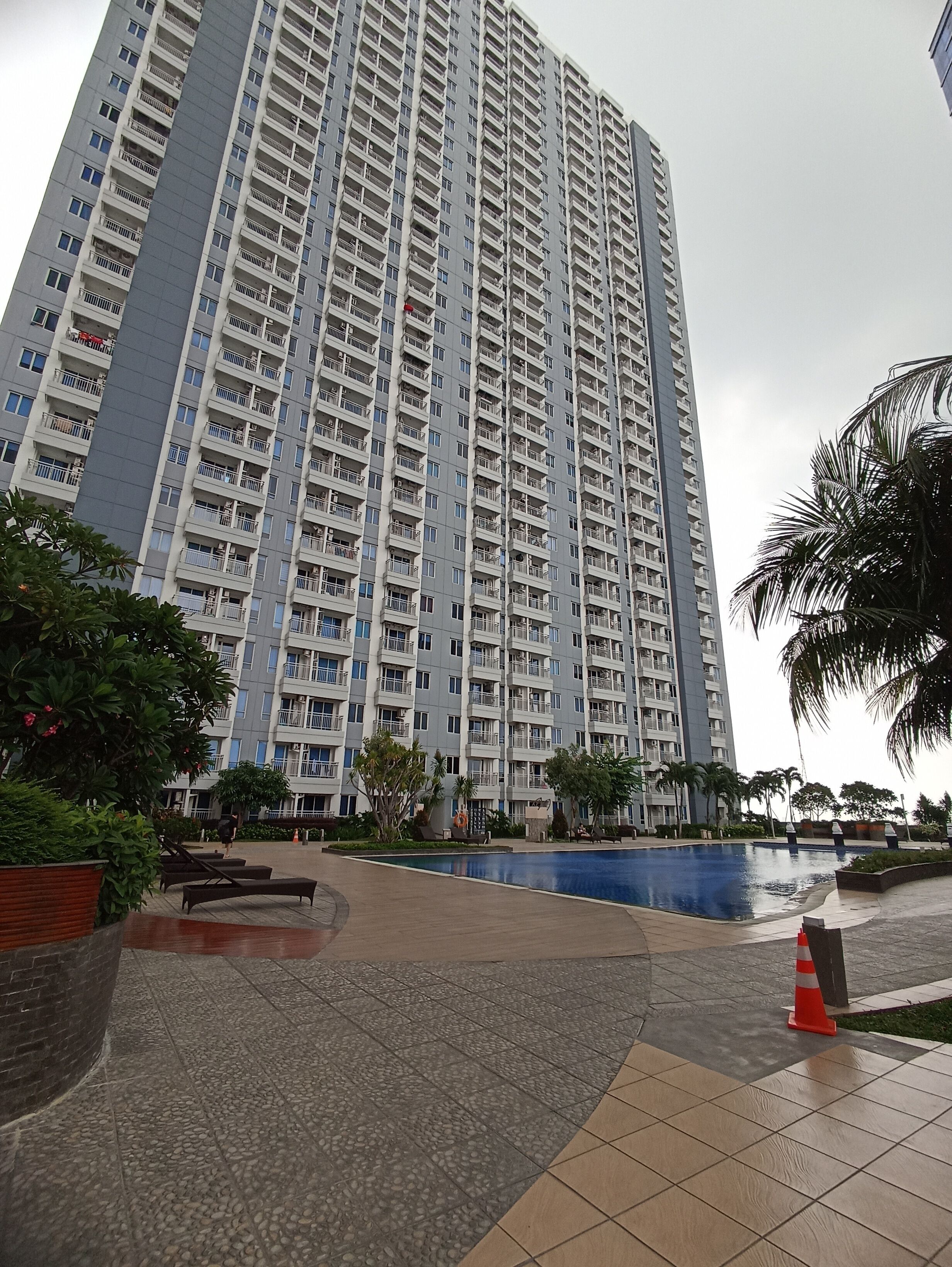 Um edifício residencial alto com várias varandas, piscina e áreas verdes ao redor.