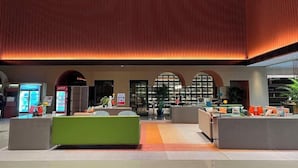Um lobby moderno com teto alto, balcão de recepção, áreas de estar e uma grande janela com vista para o exterior.