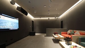 Interior moderno com uma tela grande, área de estar e uma mesa com garrafas e frutas.