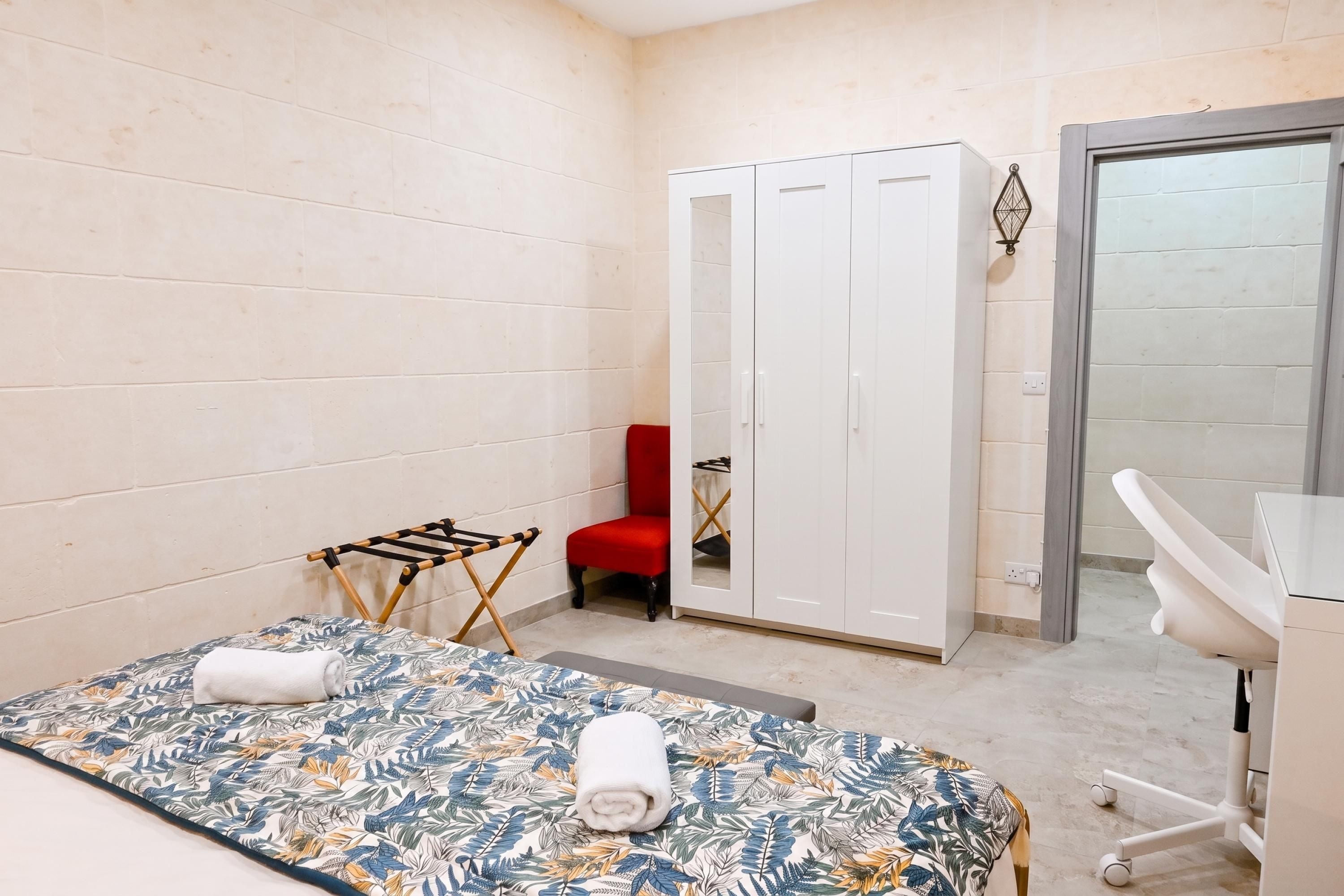 Quarto pequeno e limpo, com cama, guarda-roupa, cadeira e escrivaninha.