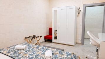 Quarto pequeno e limpo, com cama, guarda-roupa, cadeira e escrivaninha.