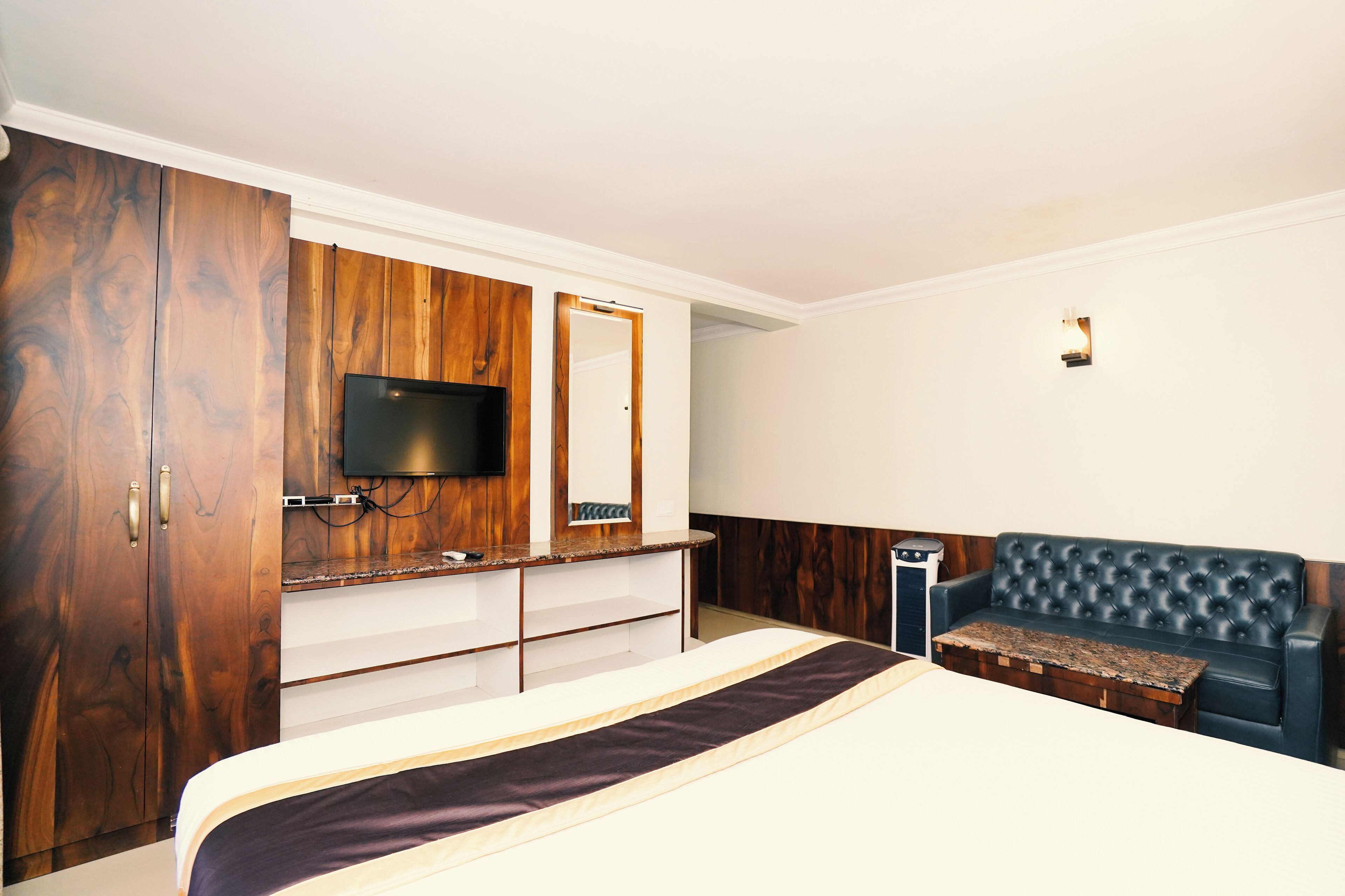 Quarto com uma cama grande, guarda-roupa de madeira, televisão, sofá e uma pequena mesa.