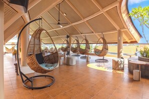 Uma área de estar ao ar livre ampla, com cadeiras suspensas e piso de azulejos.