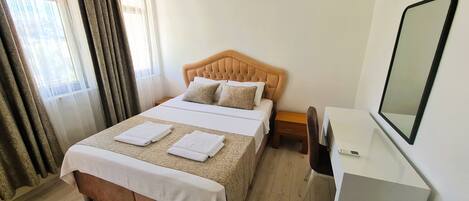 Uma cama bem arrumada com cabeceira, mesa de cabeceira, espelho e janela com cortinas.