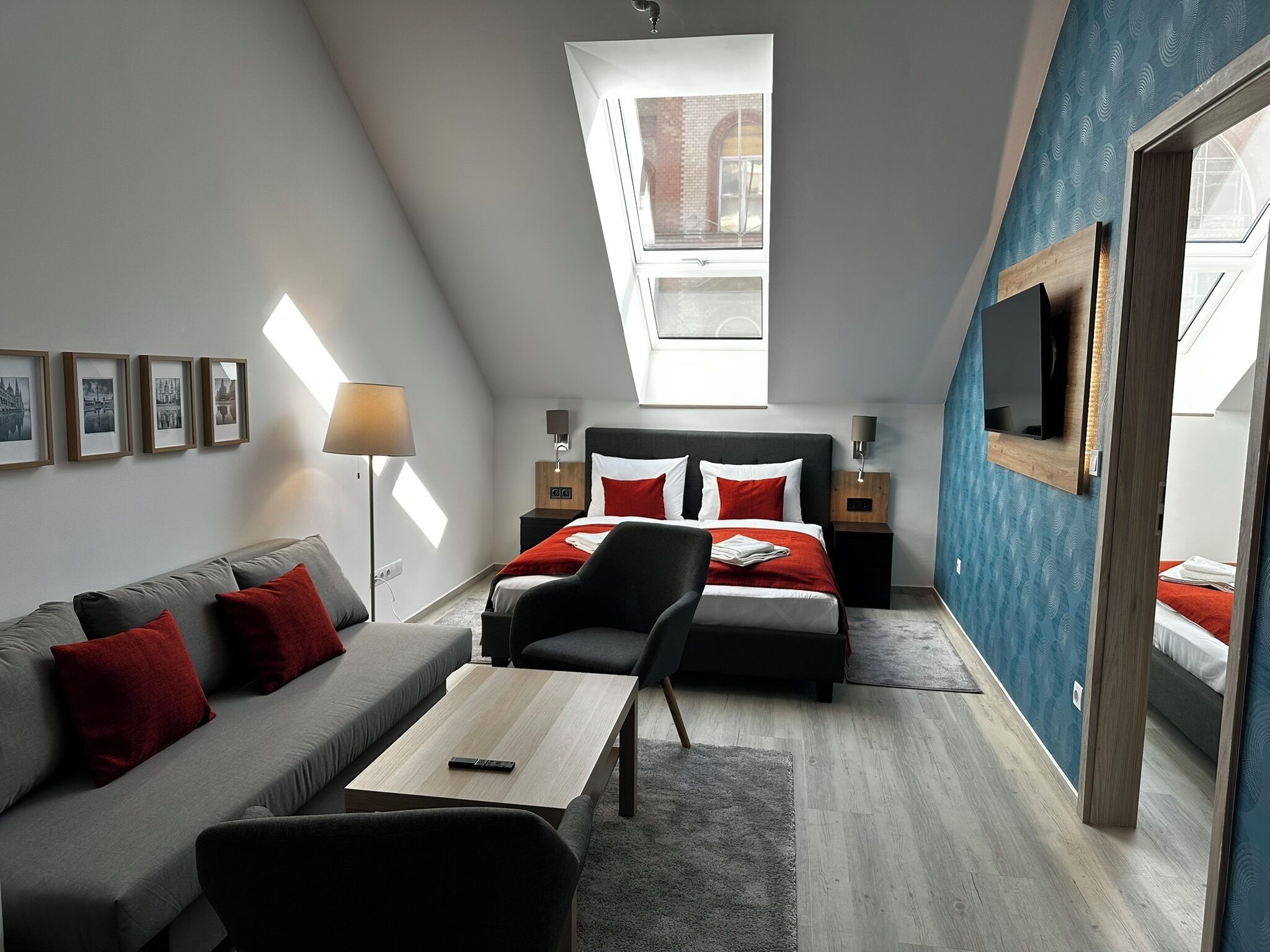 Quarto de hotel moderno com cama beliche, sofá, mesa de centro e televisão fixada na parede.