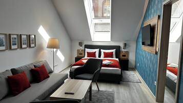 Quarto de hotel moderno com cama beliche, sofá, mesa de centro e televisão fixada na parede.