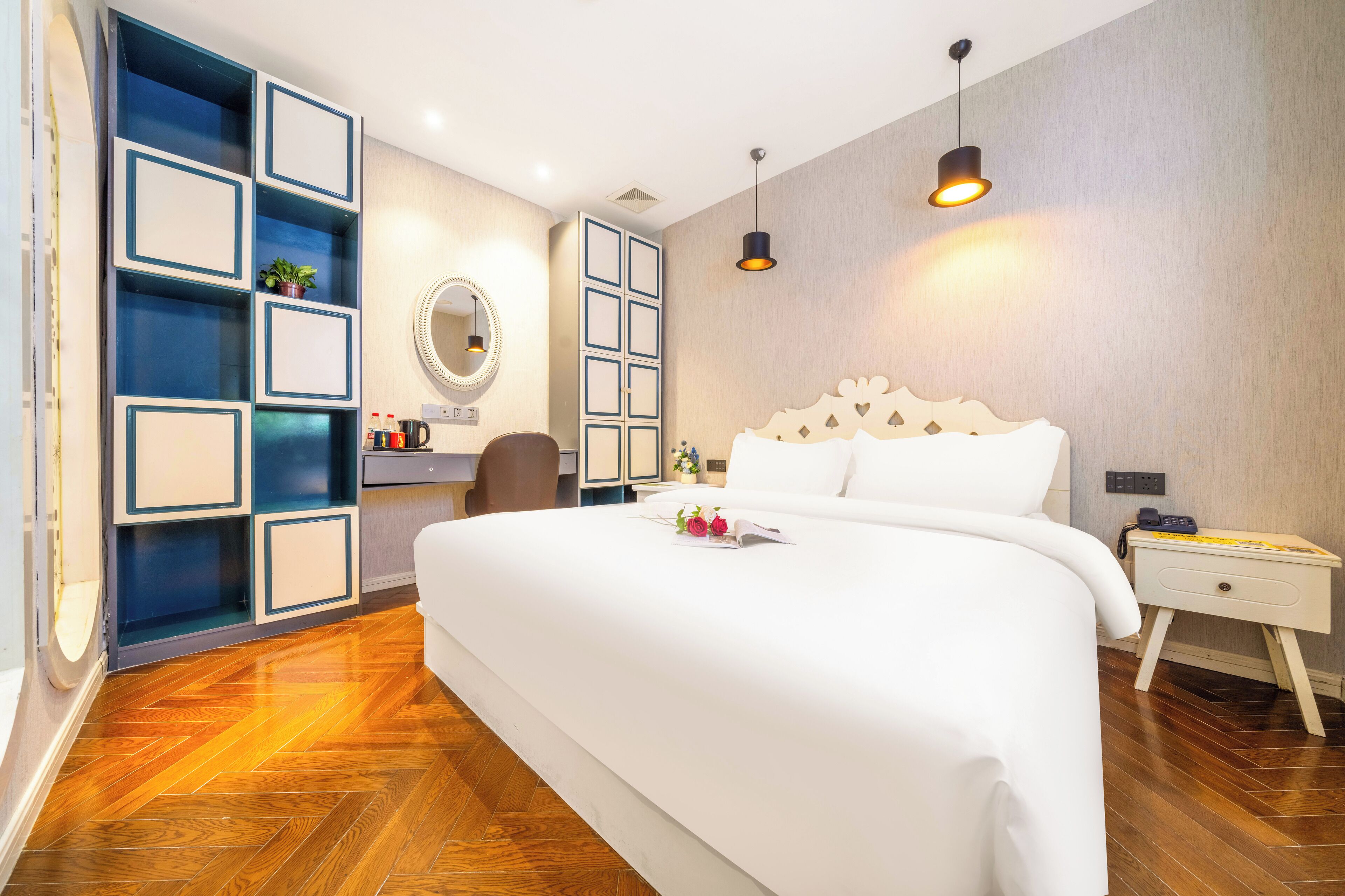 Quarto de hotel moderno com uma cama grande, uma mesa de cabeceira, uma cadeira, uma escrivaninha, um espelho e uma estante azul.