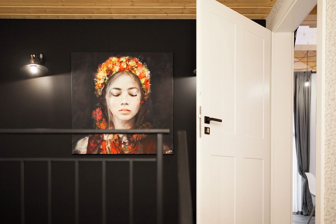Um corredor com parede preta, porta branca e um quadro emoldurado acima da porta.