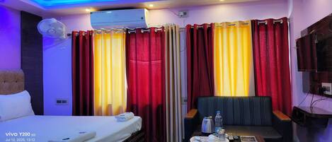 Quarto de hotel com uma cama, um sofá, uma mesa com uma bandeja de objetos e uma televisão na parede.