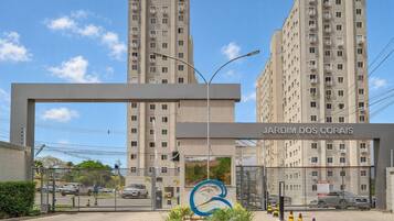 Uma entrada gradeada para um complexo de edifícios residenciais com vários prédios altos, céu claro e um logotipo no centro.