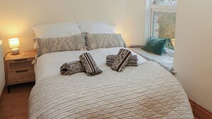 Quarto com cama, almofadas, mesa de cabeceira, luminária e duas fotos emolduradas na parede.