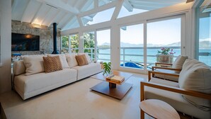 Sala de estar moderna com lareira de pedra, janelas amplas com vista para o mar, um sofá e uma mesa de centro.
