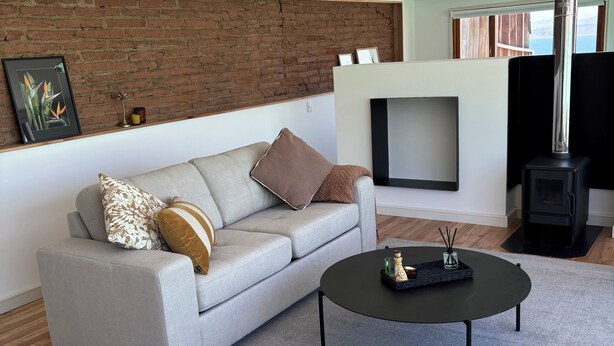 Uma sala de estar moderna com um sofá cinzento, uma mesa de centro redonda e uma parede de tijolos.