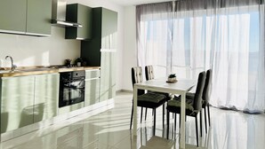 Cozinha moderna com área de refeições, apresentando uma grande janela com cortinas leves, forno embutido e mesa de jantar com cadeiras.