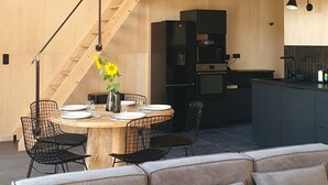 Uma sala de estar ampla com teto alto, mesa de jantar com cadeiras, sofá e área de cozinha com escada.
