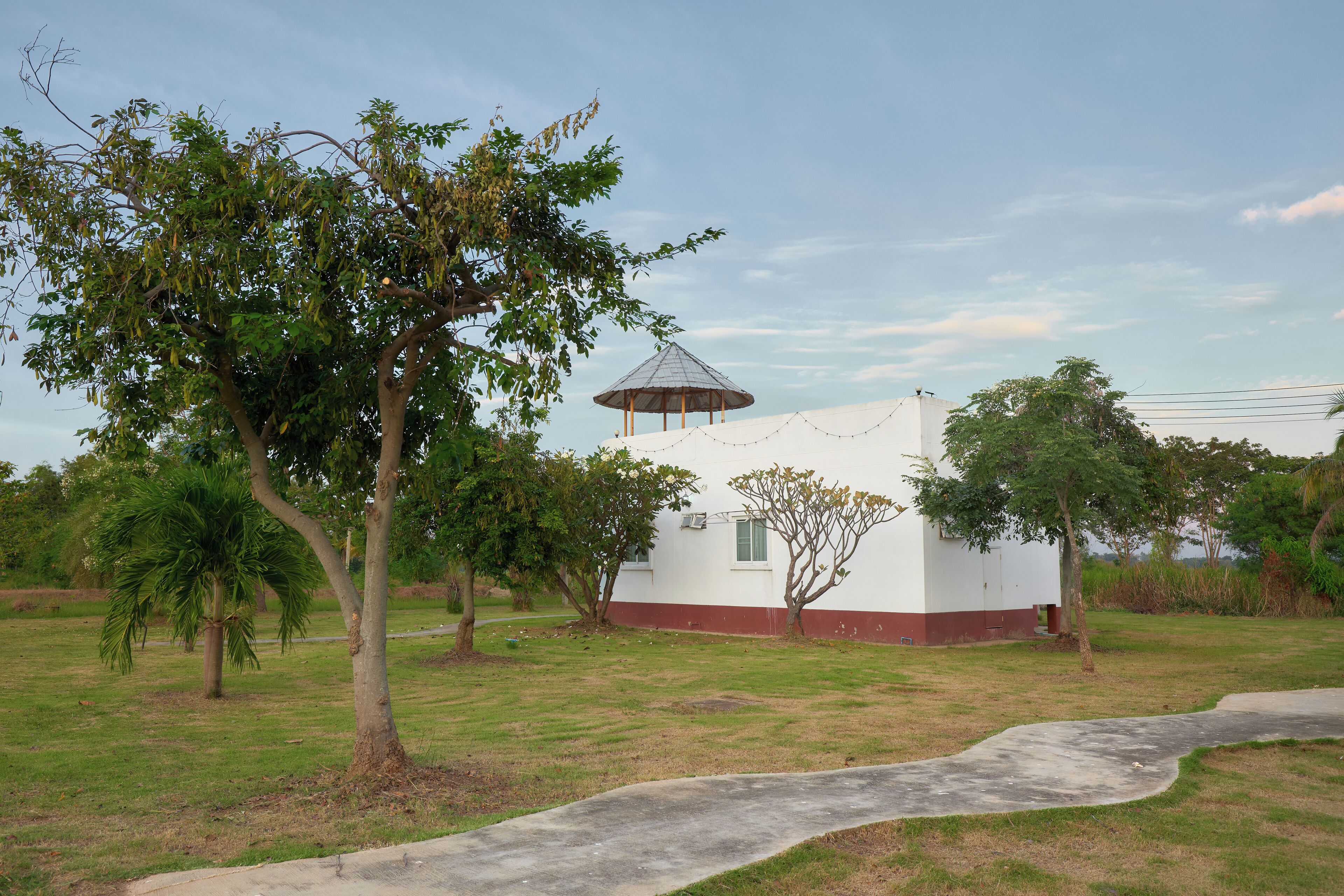 Um edifício branco com base vermelha, cercado por árvores e um caminho de concreto.