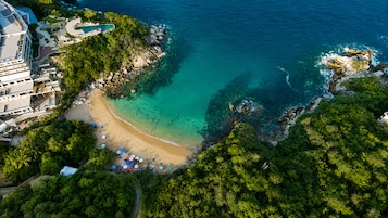 Vista aérea de um resort costeiro com piscina, praia e vegetação exuberante.
