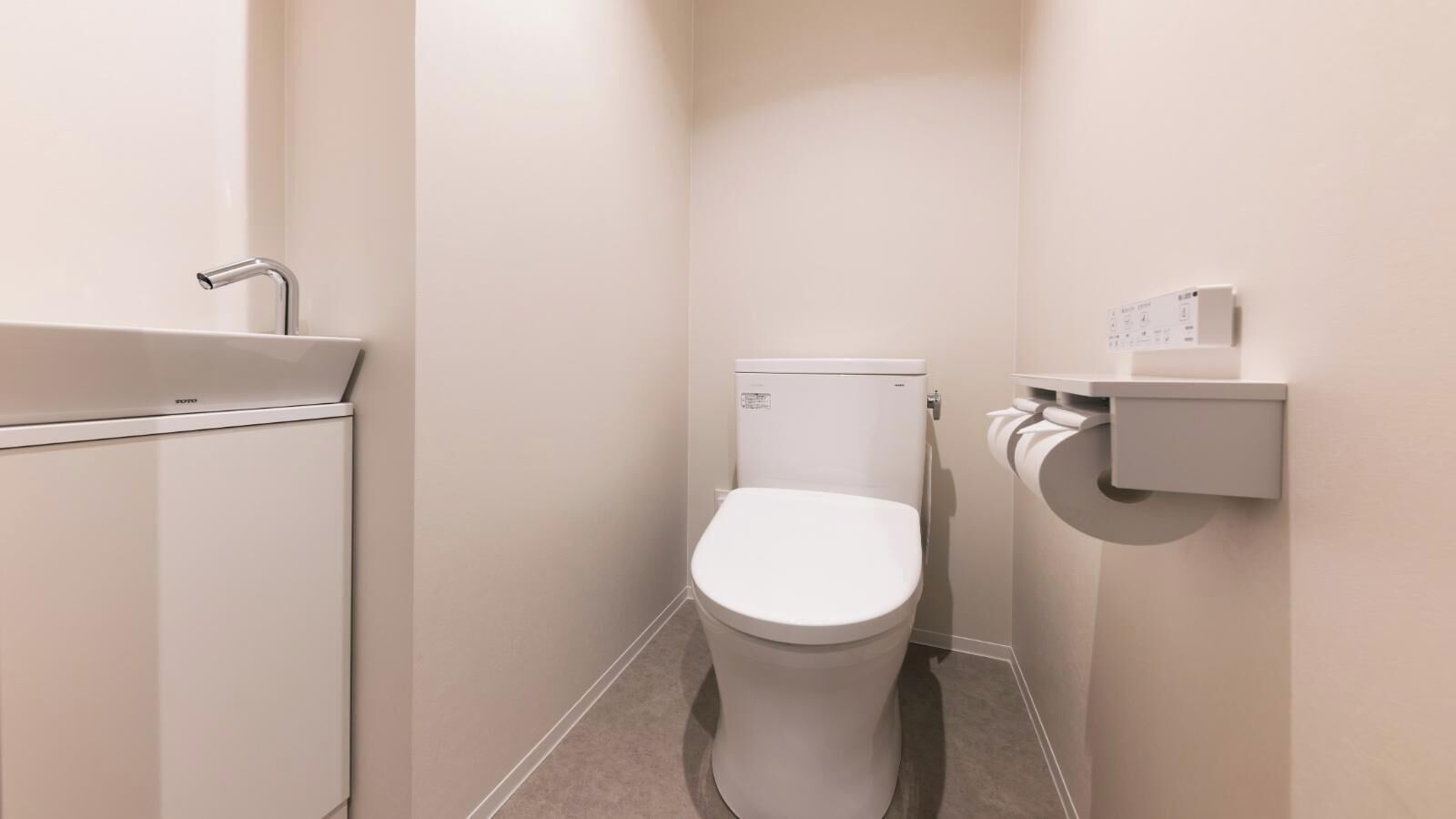 Uma casa de banho pequena e moderna com sanita, lavatório e suporte para rolo de papel higiénico.