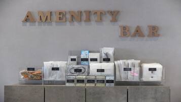 Exposição de comodidades no Amenity Bar, incluindo diversos produtos embalados e uma caixa de plástico transparente com itens.