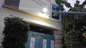 Um edifício residencial com vários andares, entrada com portão, um pequeno jardim e escadaria visível que leva à entrada.