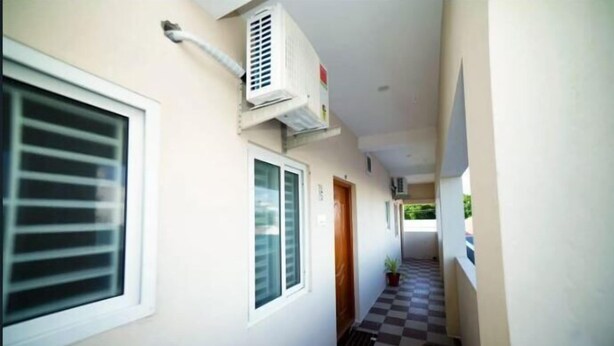Um corredor com piso xadrez, uma janela com persianas e um aparelho de ar condicionado fixado na parede.