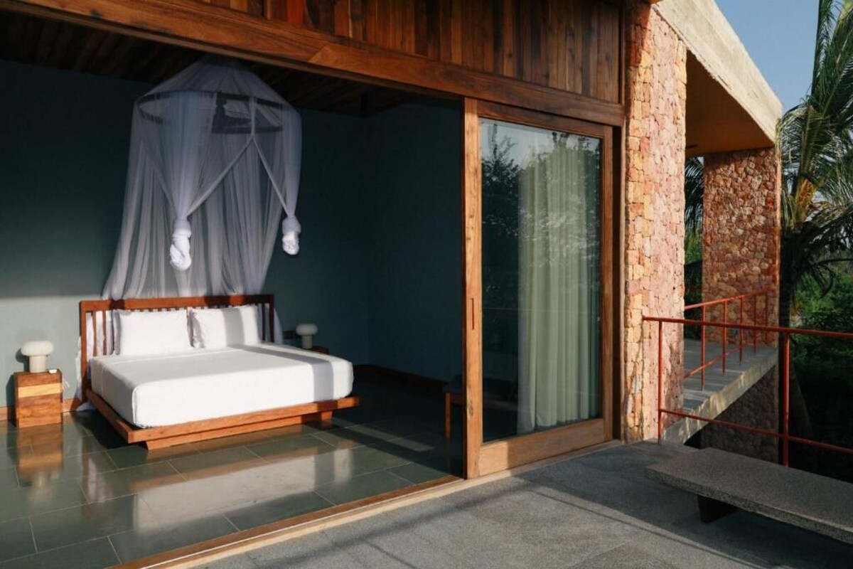 Quarto com cama, mesa de cabeceira, janela e escada que dá para o exterior.