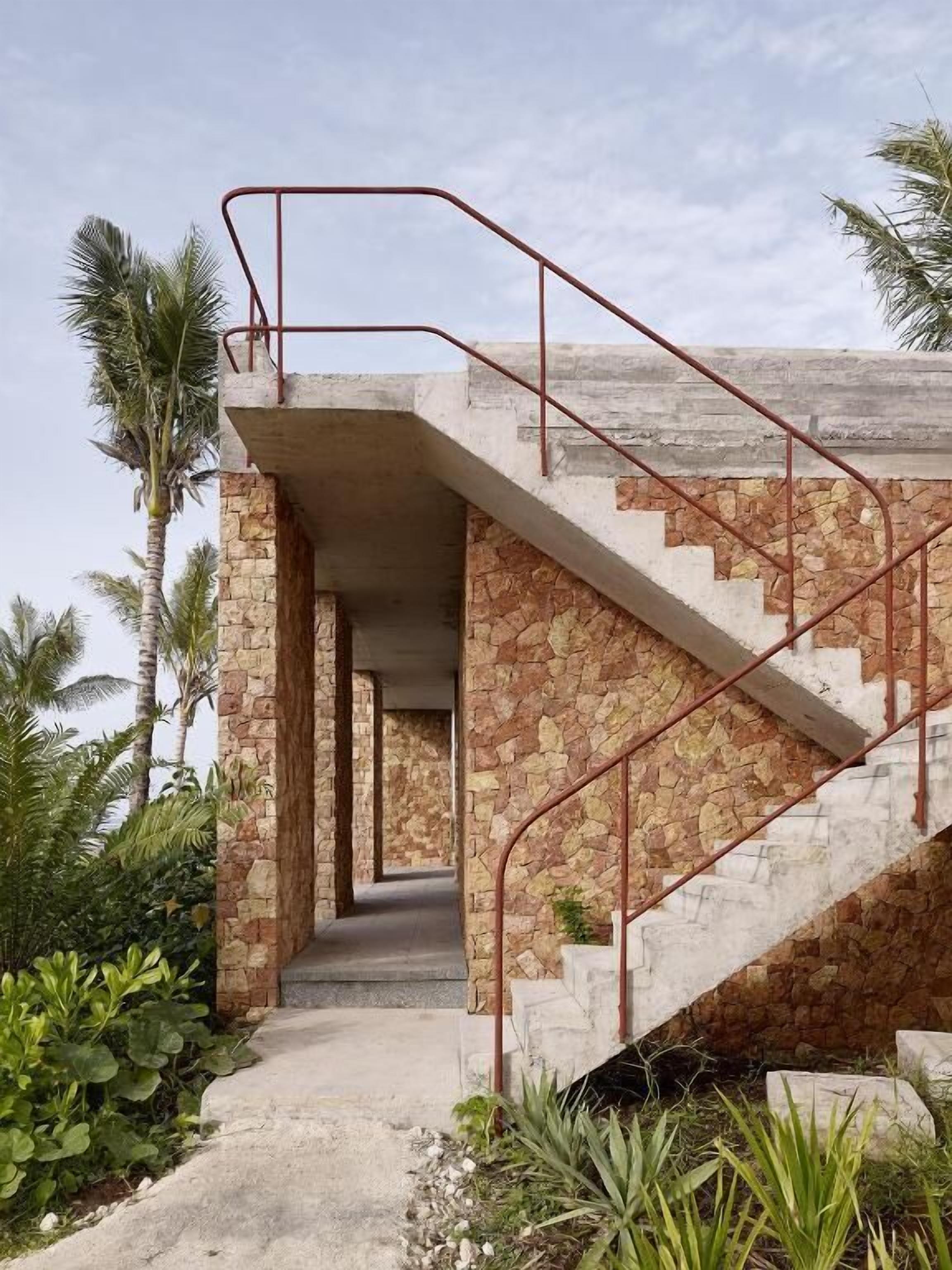 Escadaria que leva a um nível superior de concreto com uma parede de pedra de um lado, cercada por vegetação.
