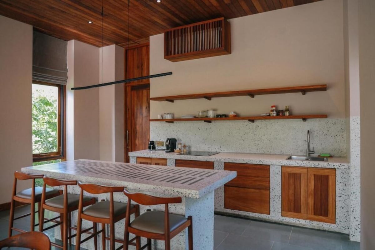 Cozinha com ilha central, cadeiras de madeira e prateleiras embutidas.